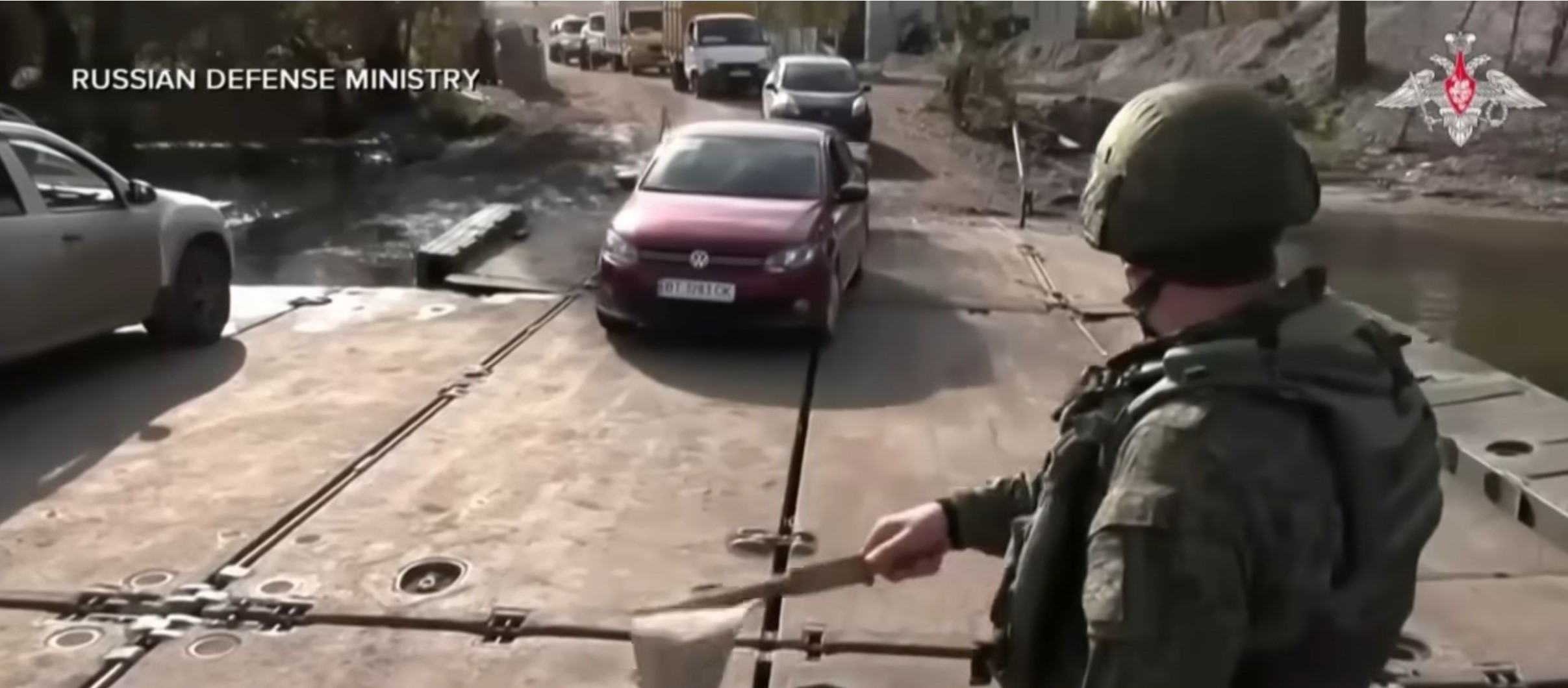 A Russian soldier guides vehicles over a temporary bridge as they ...